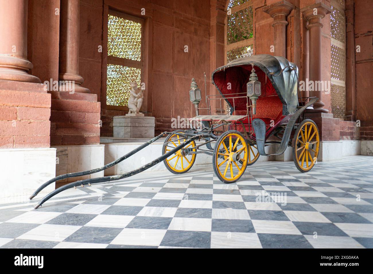An old, vintage carriage next to columns and small statues is located ...