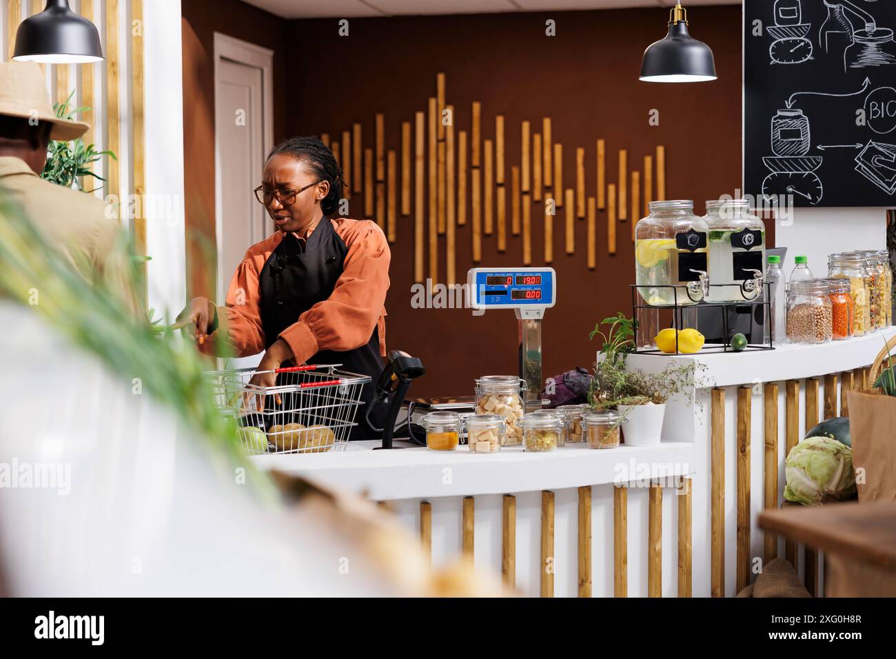 African American female cashier in a black apron gesturing to something ...