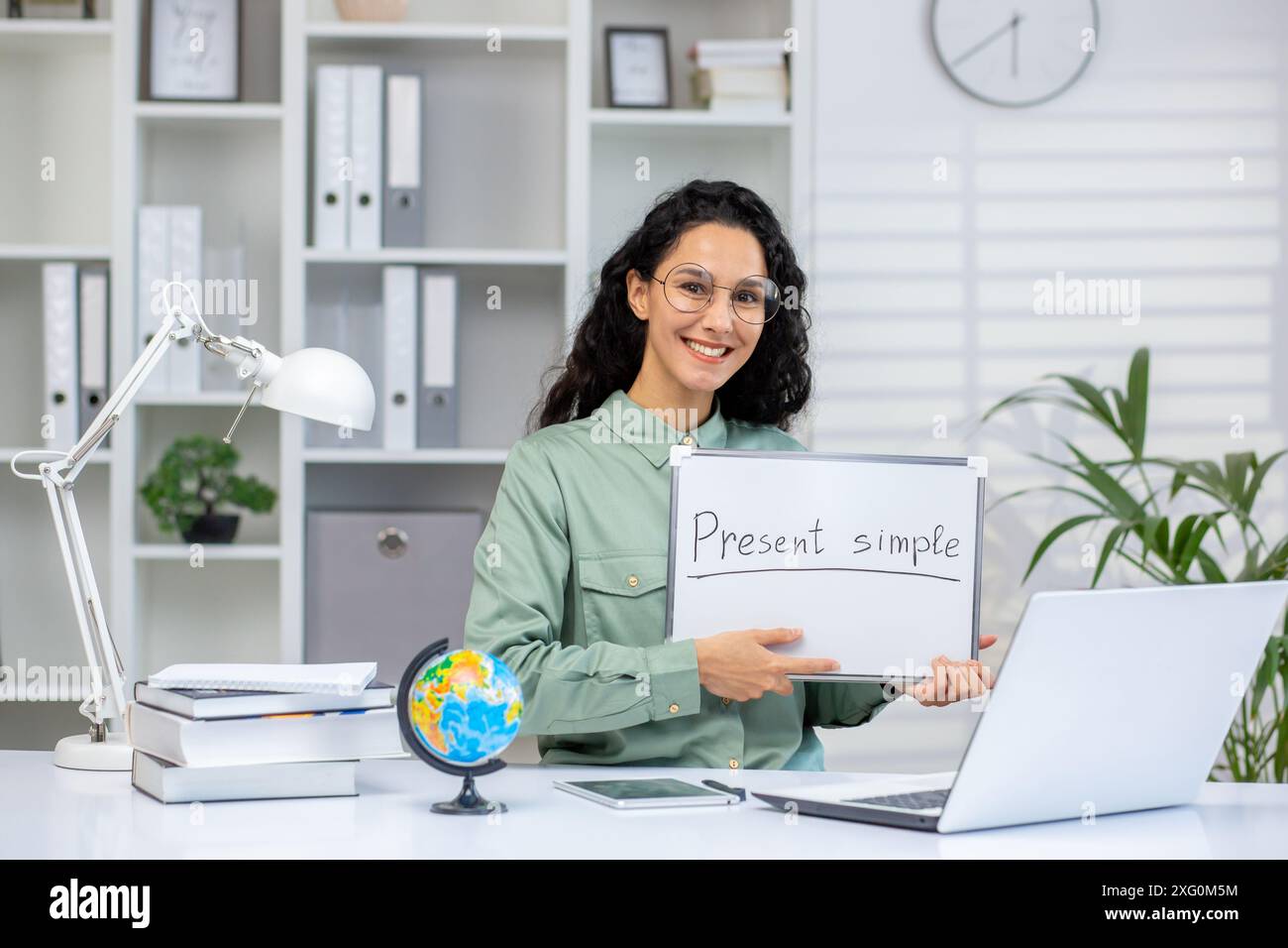 Smiling teacher holding a whiteboard with 'Present Simple' written on ...