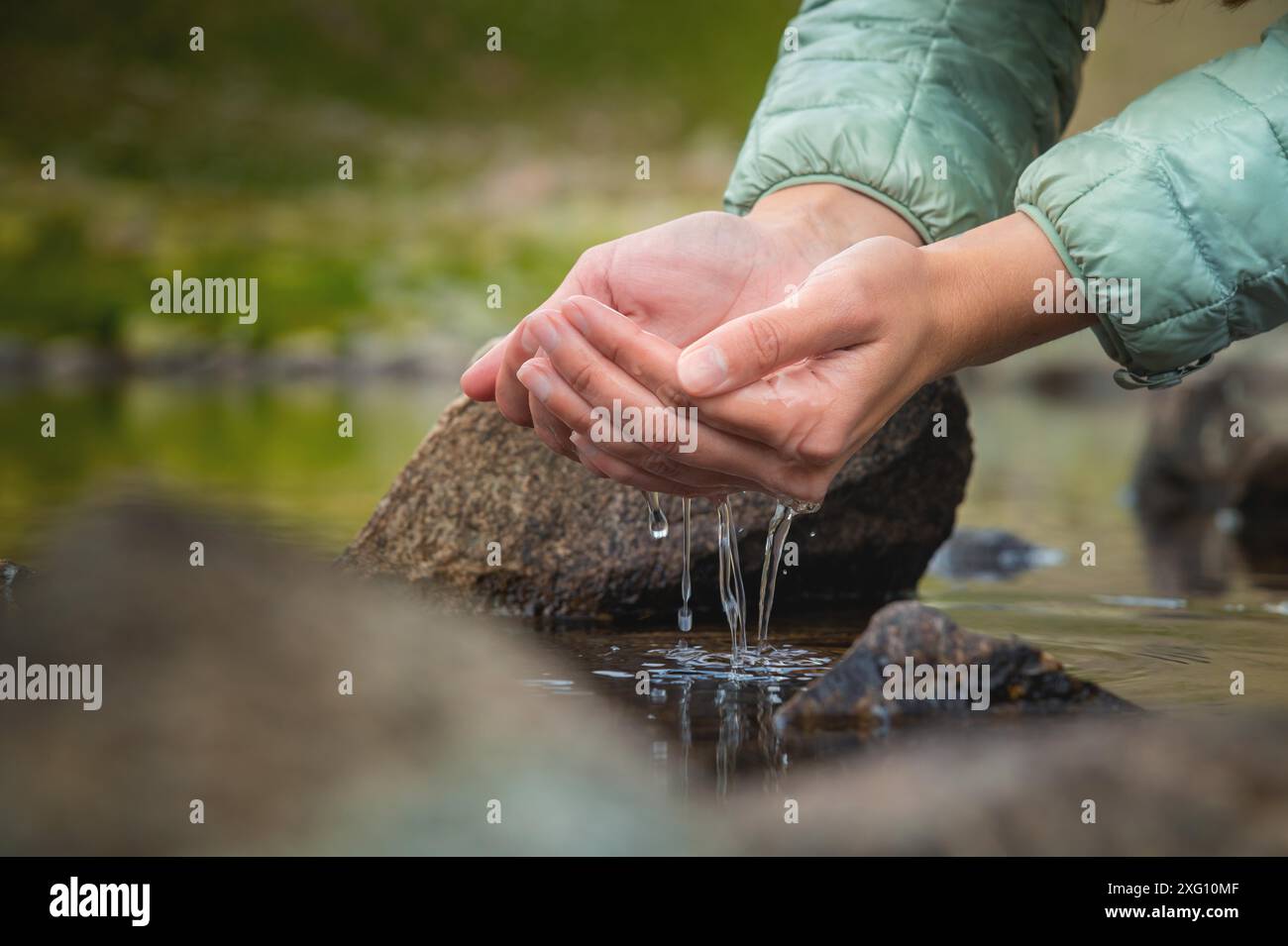 Close-up of water drops falling from female hands into a stream. The ...