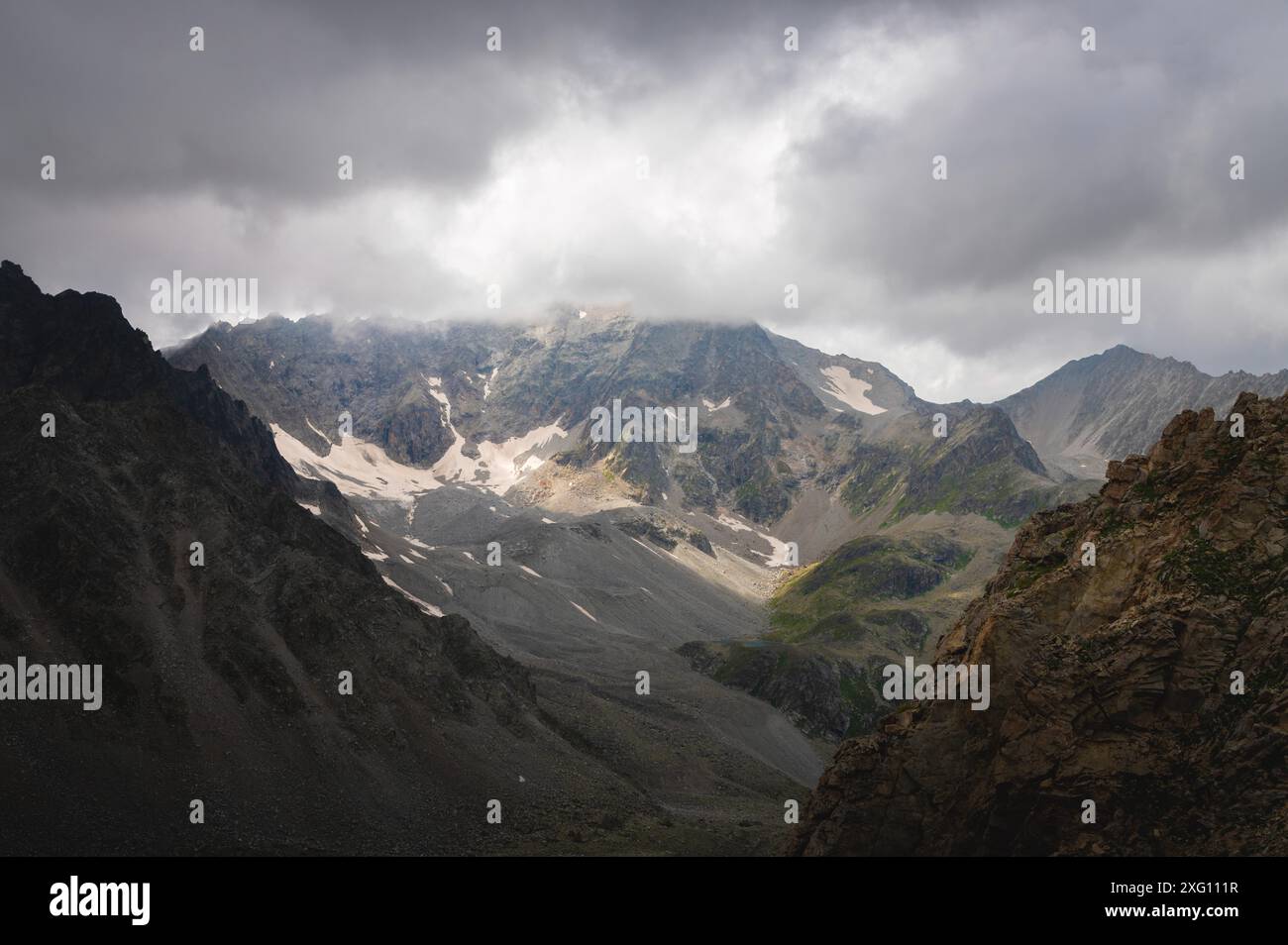 Dramatic view of forested high rocky slopes and snowy mountains in gray ...