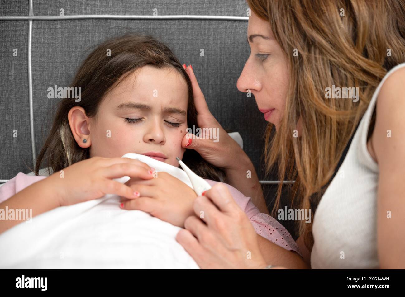 Mother measuring temperature of her ill daughter. Sick child with high fever laying in bed and ...