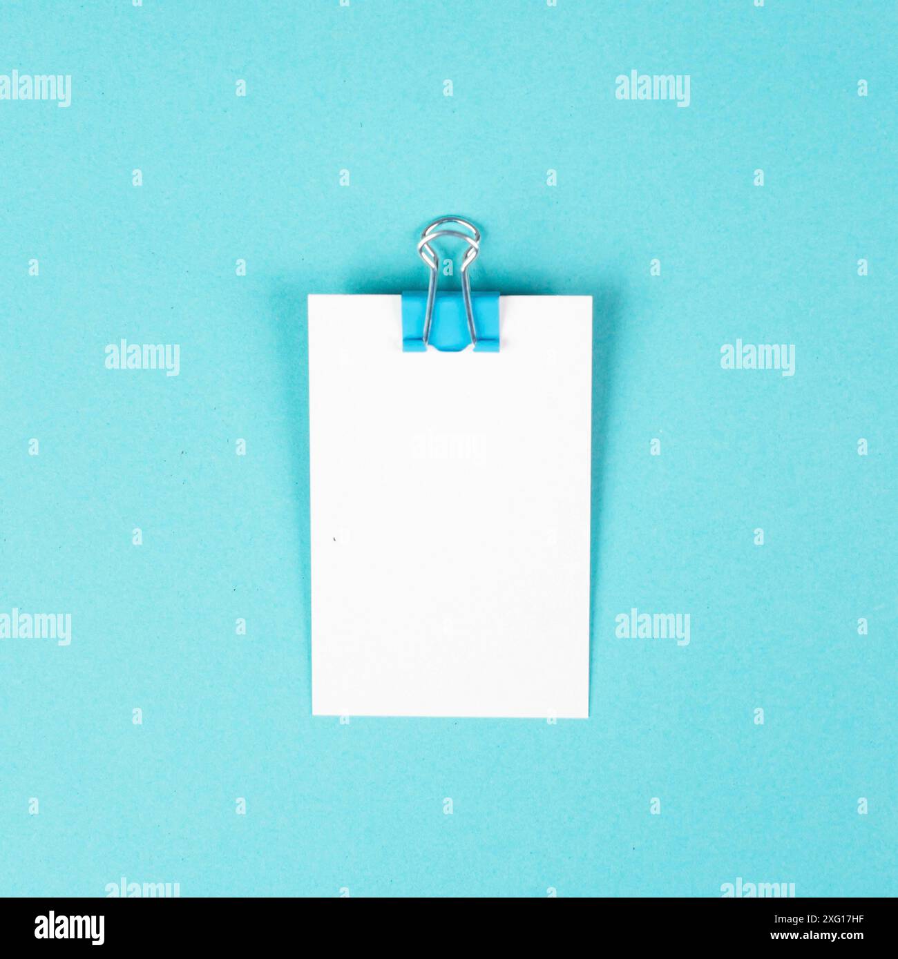 Blank white paper with a paperclip on a blue colored background, copy ...