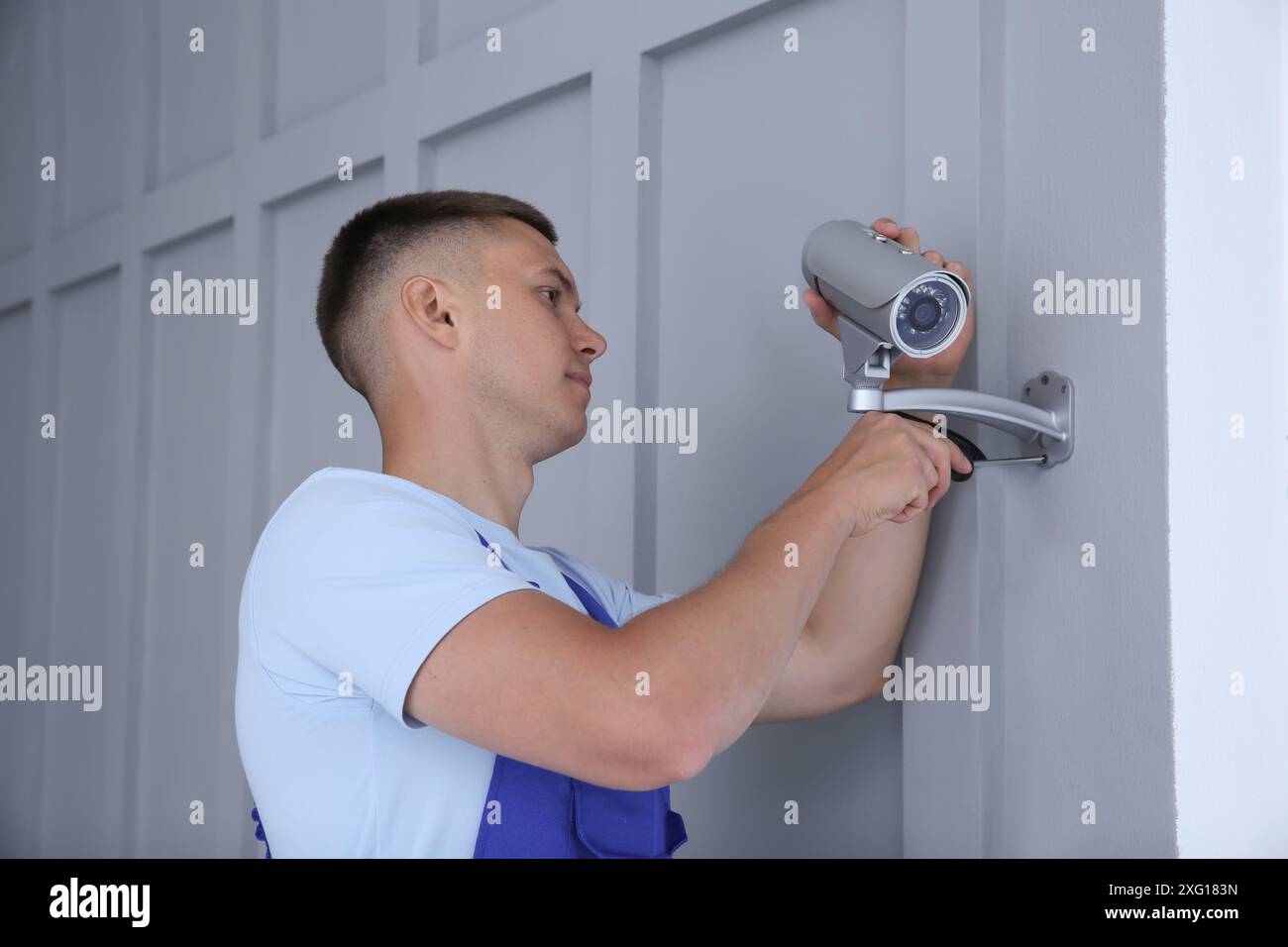 Technician with screwdriver installing CCTV camera on wall indoors ...