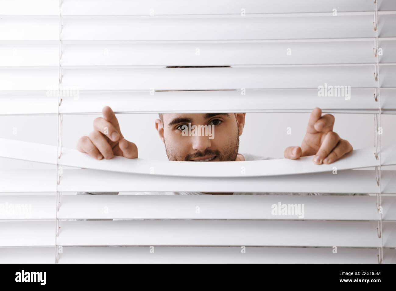 Young man looking through window blinds on white background Stock Photo ...