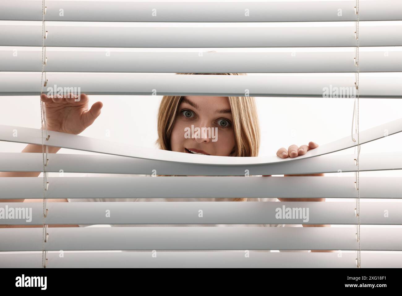 Young woman looking through window blinds on white background Stock Photo - Alamy