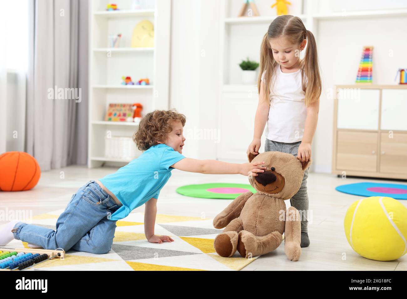 Cute little children playing with teddy bear on floor in kindergarten ...