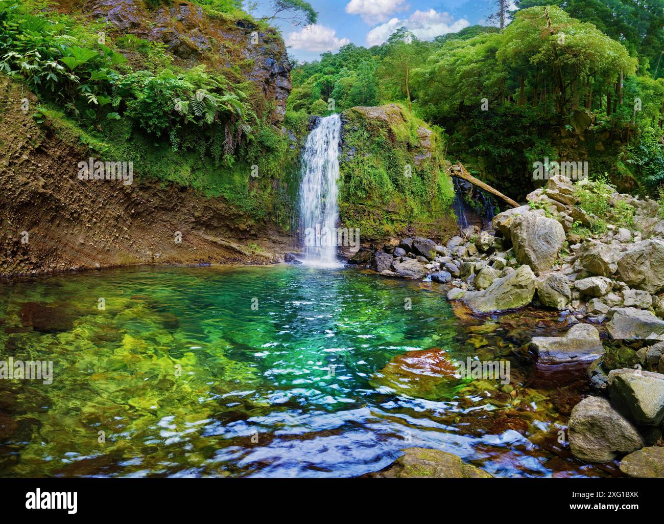 Cascading waterfall flowing into a clear green pool surrounded by rocks ...