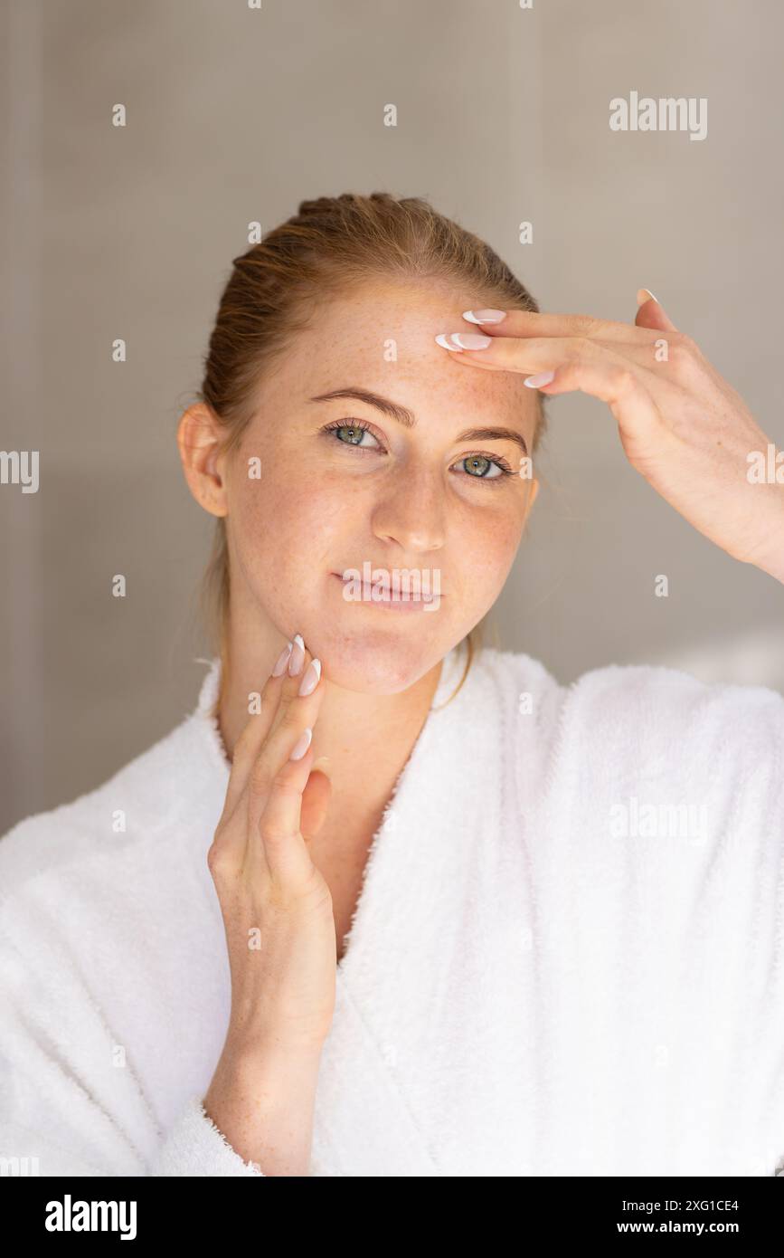 Applying skincare, woman in white robe touching face, focusing on ...