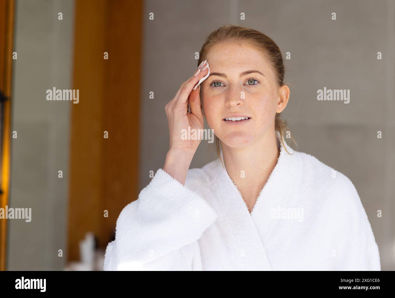 Applying skincare routine, woman in bathrobe cleansing face with cotton ...