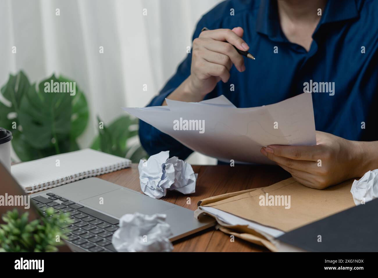 Person reviewing papers at a desk with a laptop and crumpled paper ...