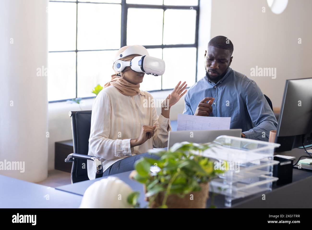 Using VR headset, business colleagues discussing project at office desk ...
