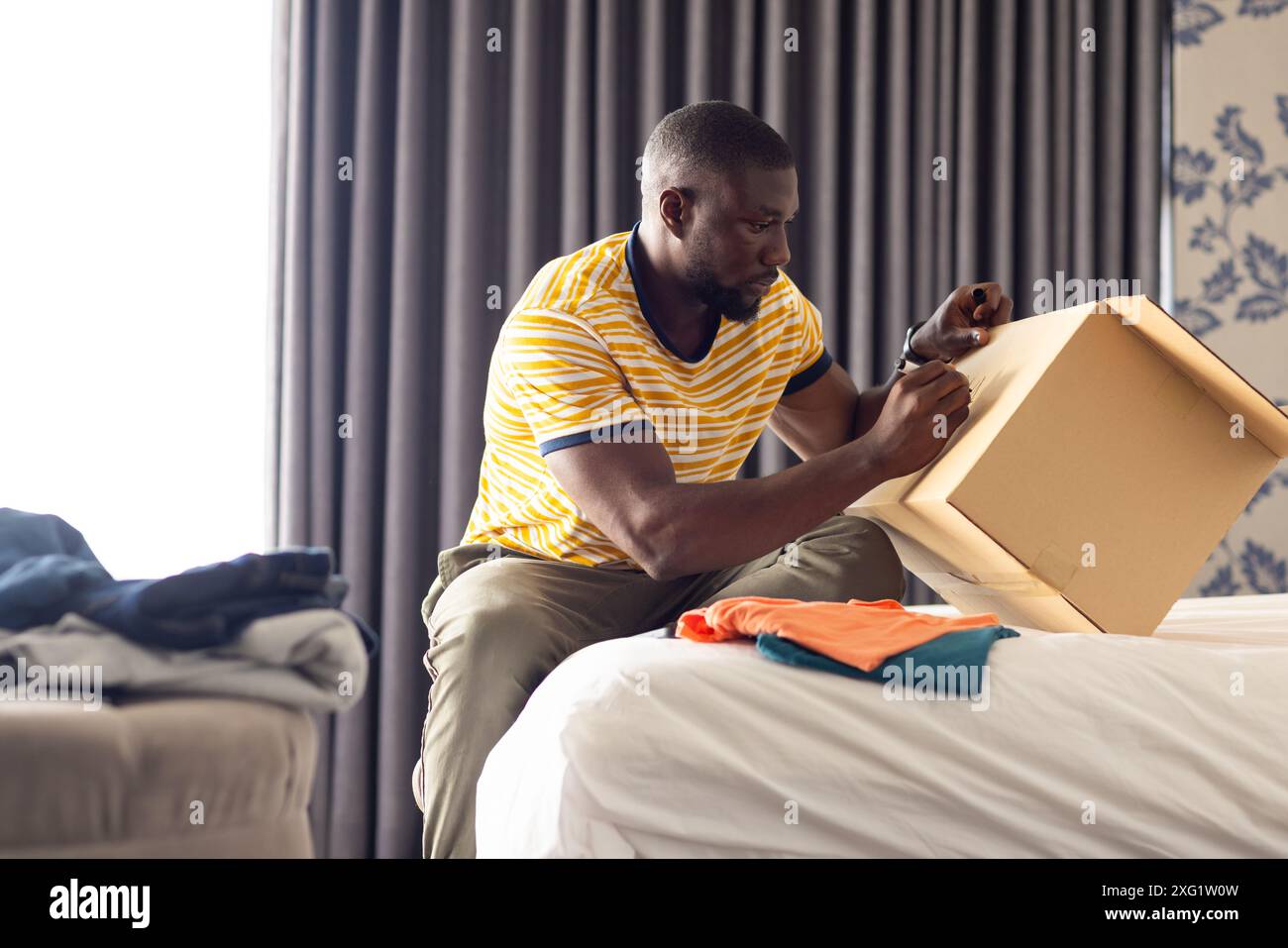 Packing cardboard box, man sitting on bed in bedroom Stock Photo - Alamy