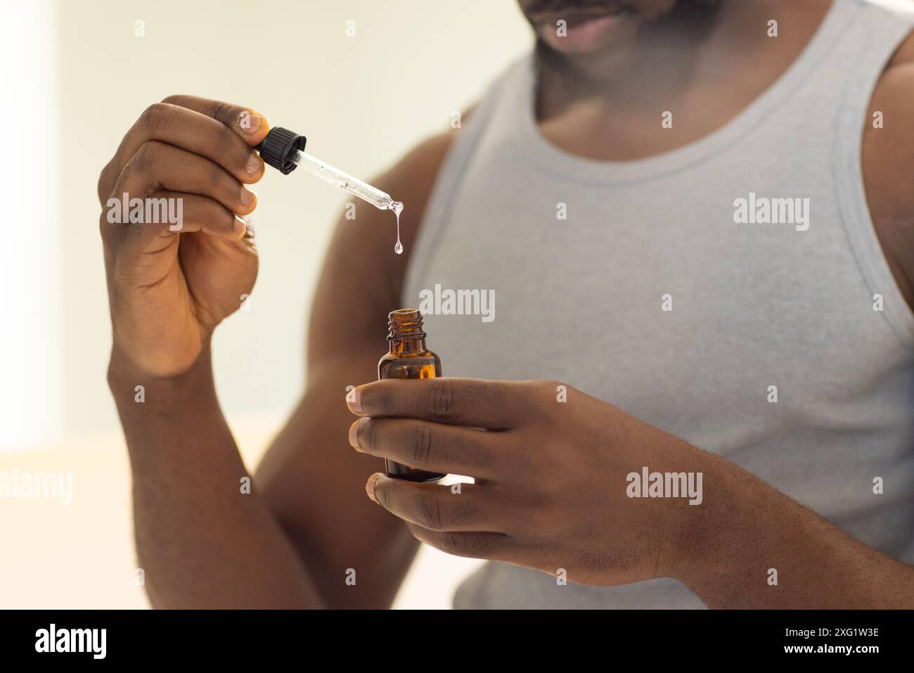 African American man using dropper bottle for skincare routine at home ...