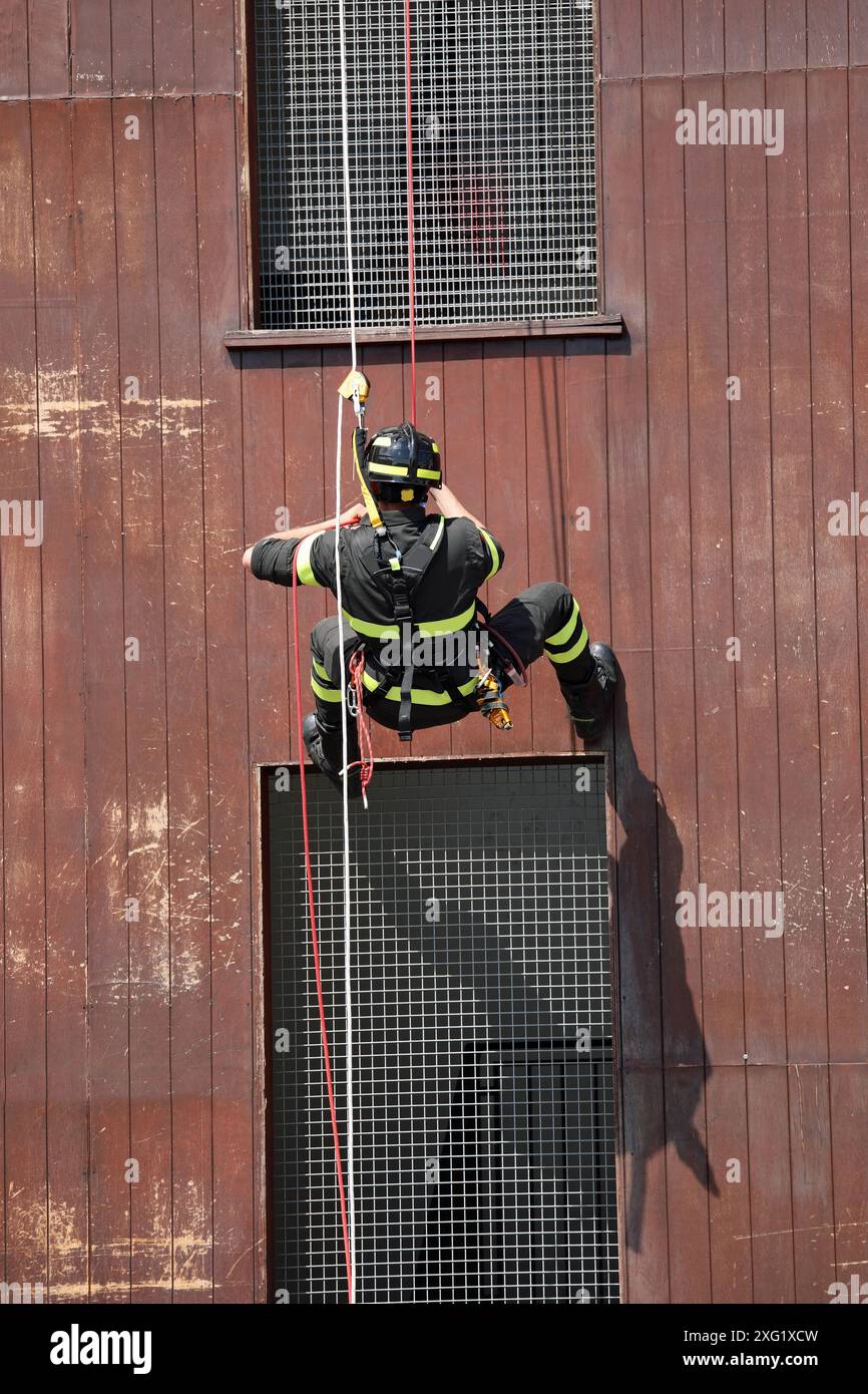 Brave firefighter in helmet and uniform rappelling down building during ...