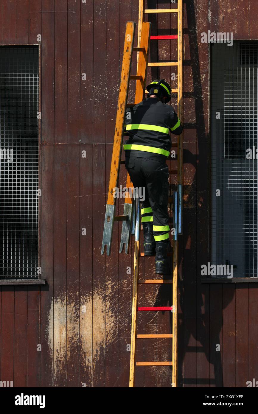 Firefighter in uniform with portective helmet climbing ladder during ...