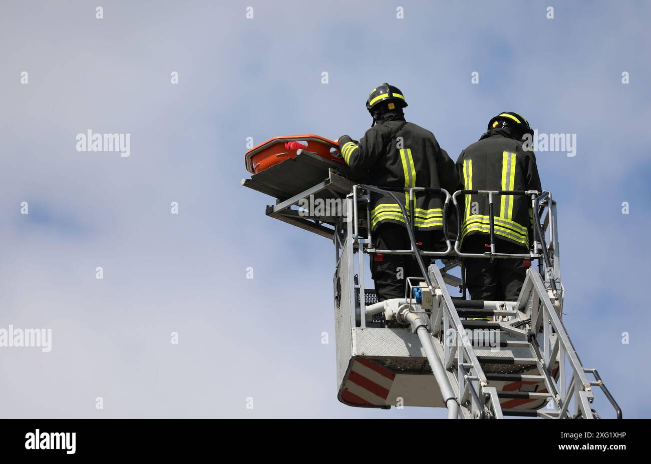 Two firefighters in the basket of the aerial ladder of fire truck ...