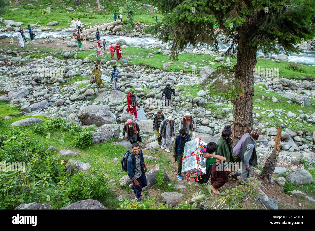 Guests from bride side carrying luggage boxes as they walk towards the groom's home along a ...