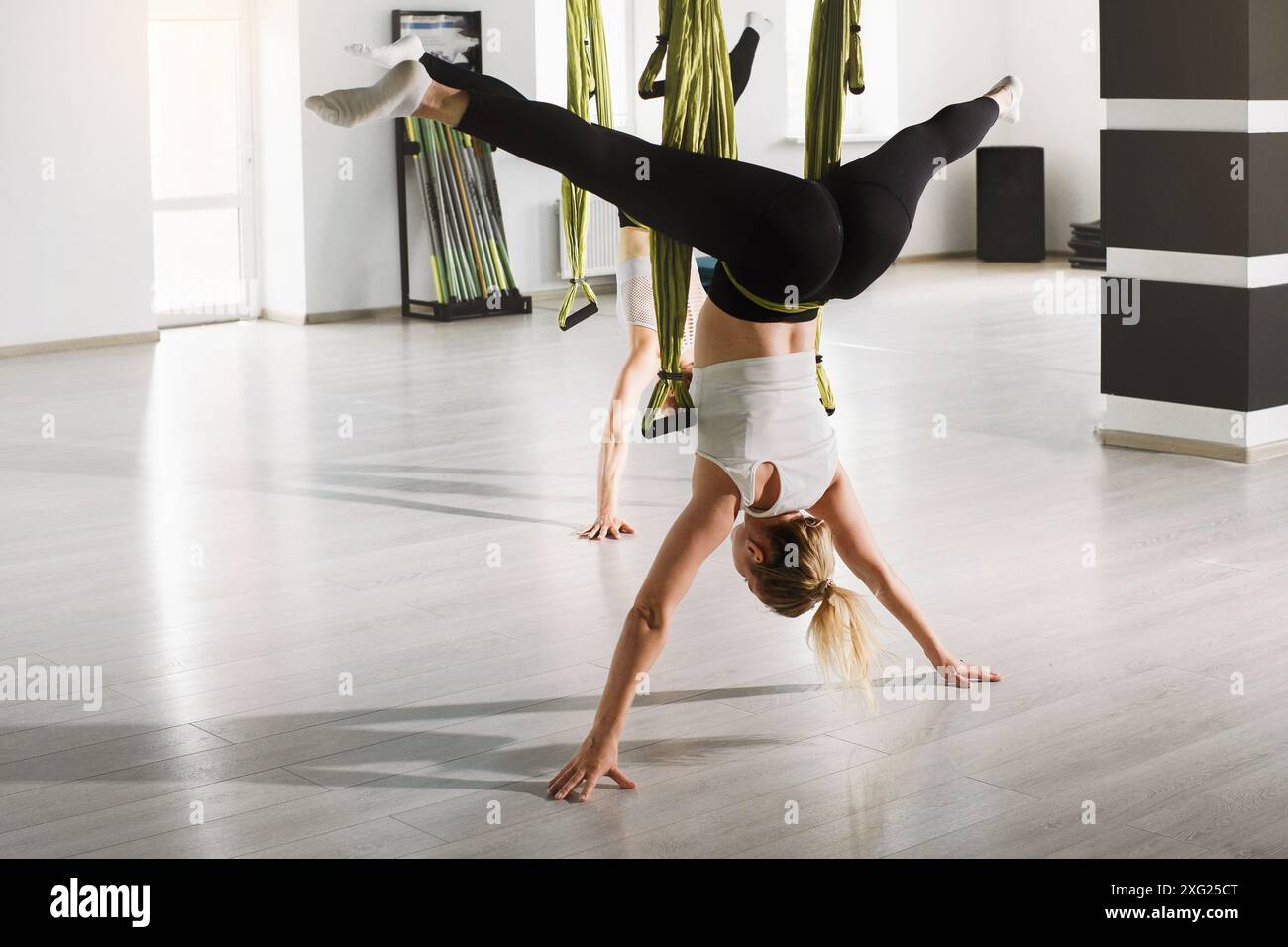 woman performs a challenging inverted pose during an aerial yoga class ...