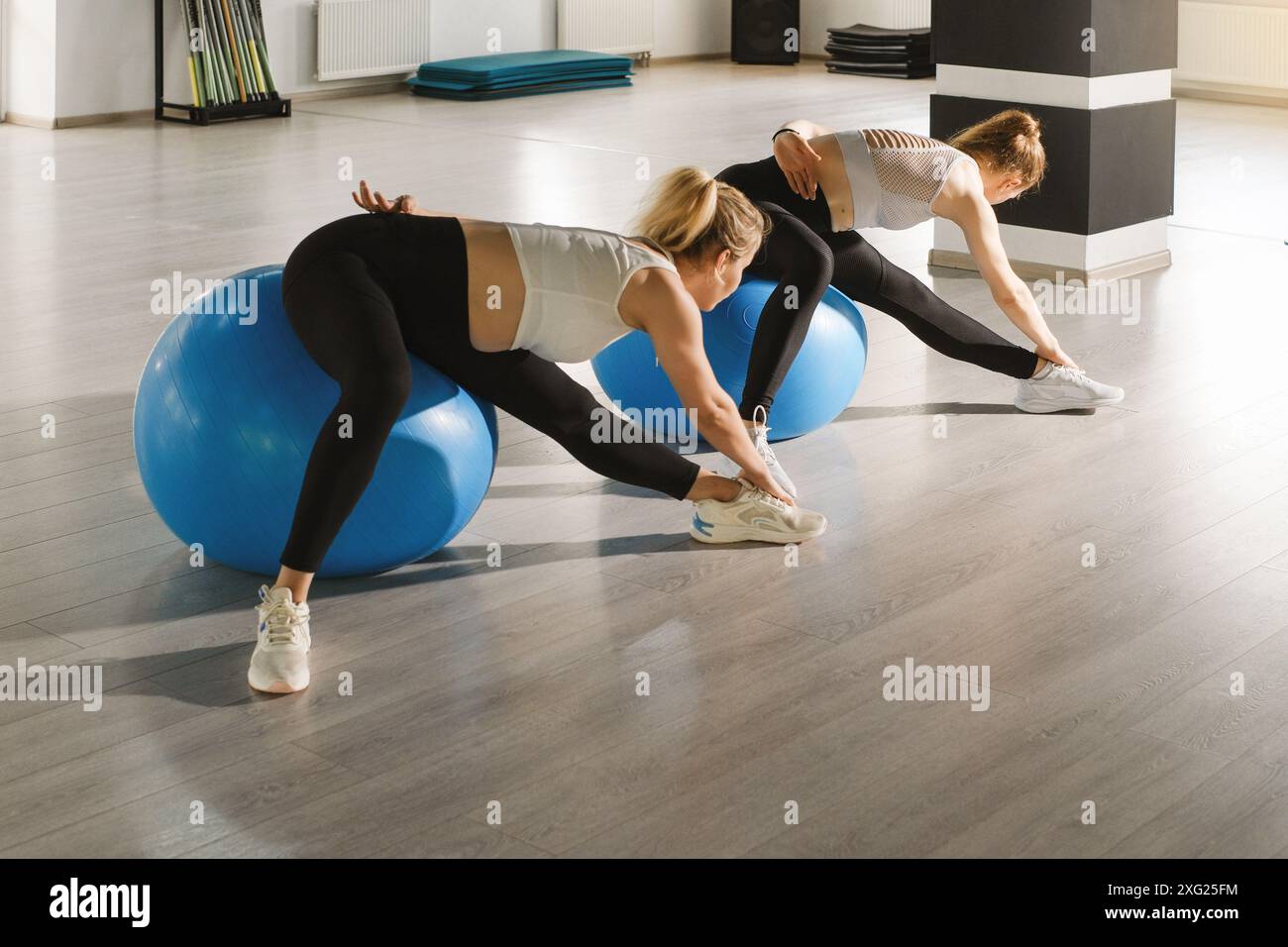 Two women in a gym doing stretching exercises on fitballs. The woman ...