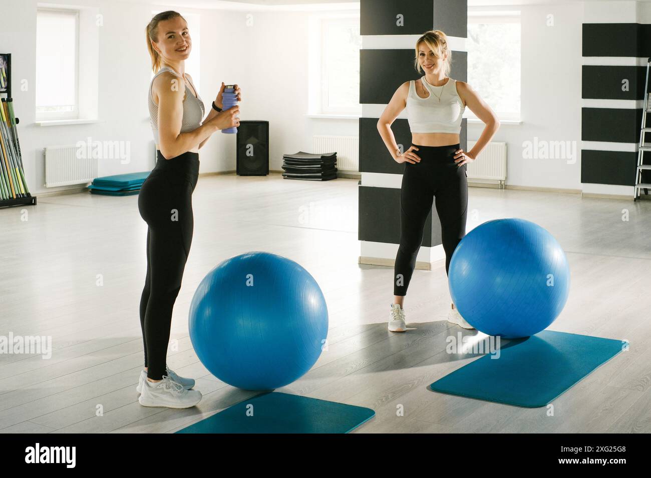 Two women in a fitness center having rest, drinking water. One woman is ...