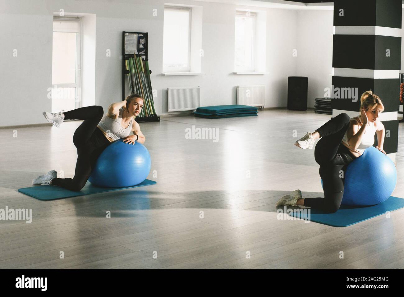 Two women perform exercise routines with fitballs in a gym setting ...