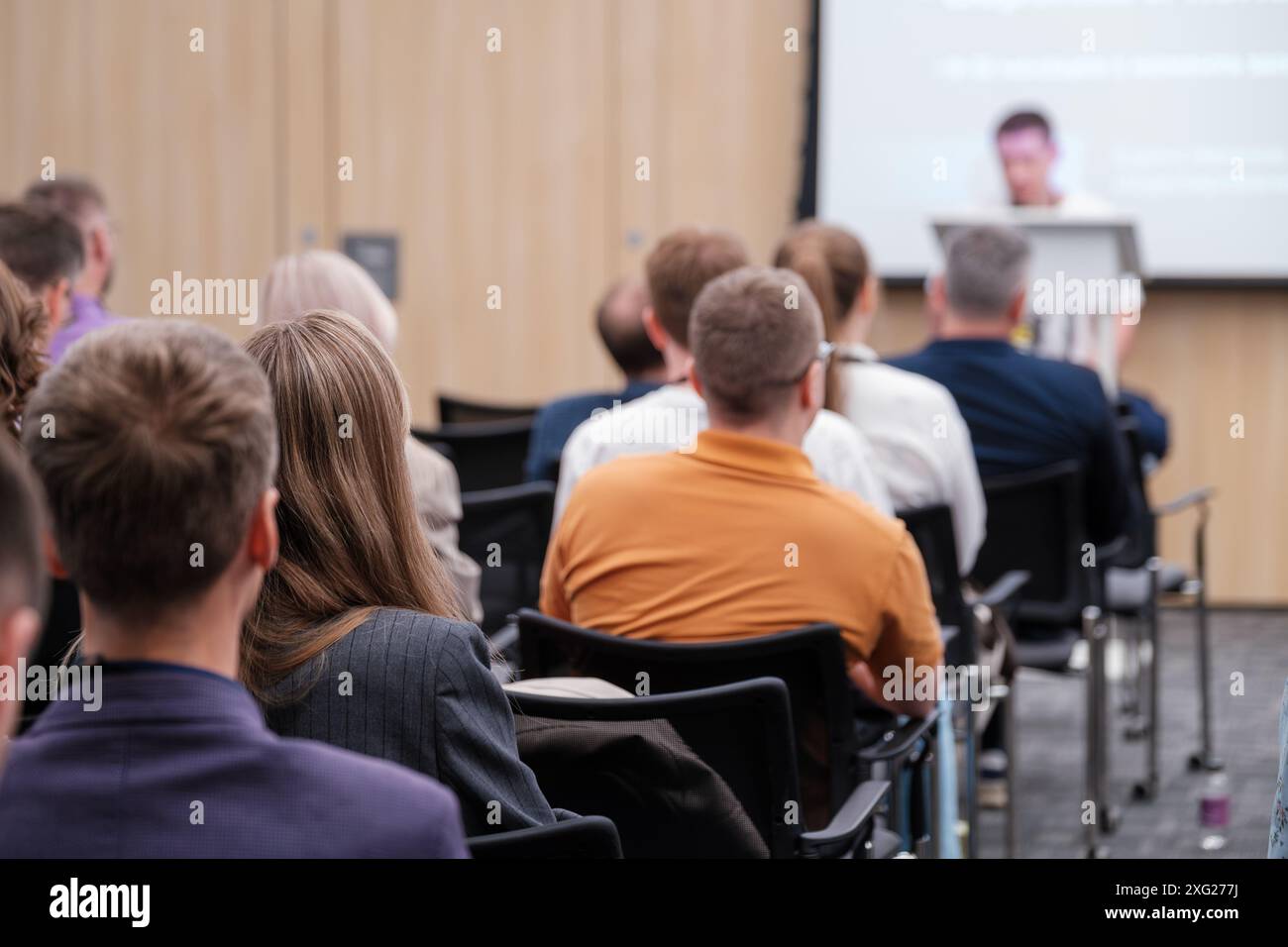 Rear view of audience members listening to a speaker at a tech ...