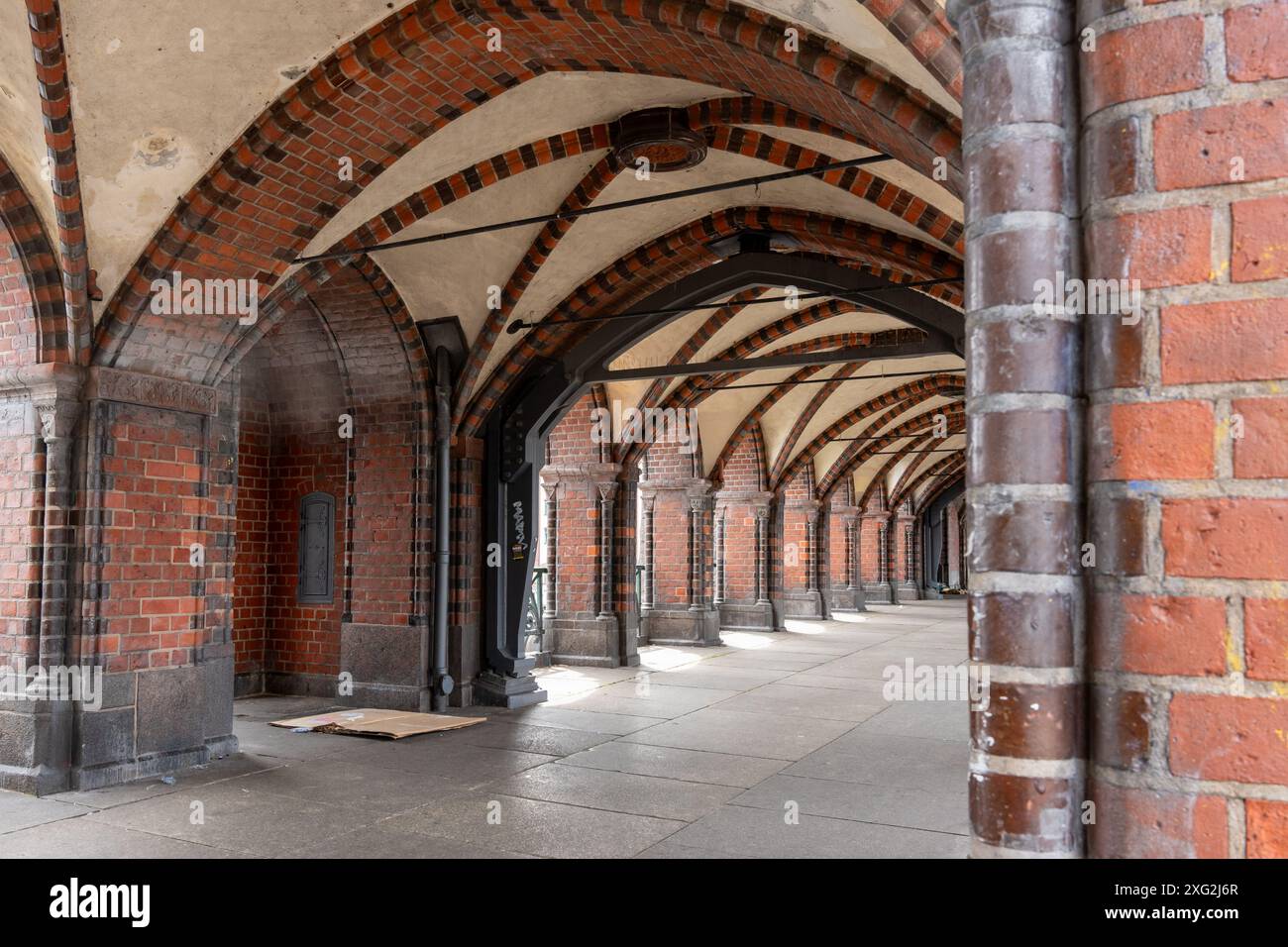 A long, narrow brick hallway with arched openings. The arches are brown ...
