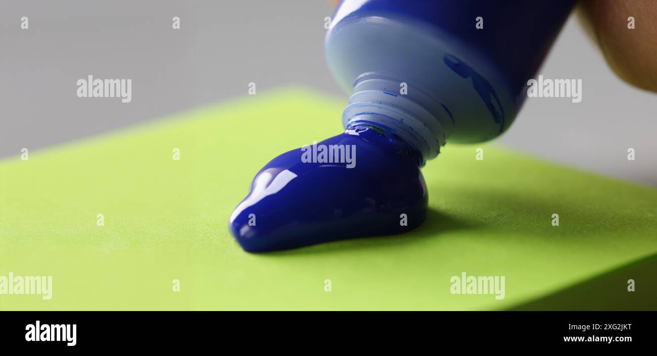 Man artist squeeze paint out of tube, bright blue colour on green paper ...