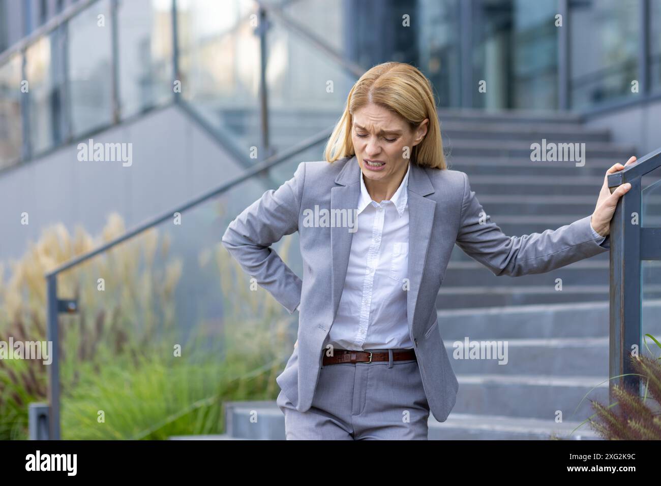 A woman in business attire experiencing back pain while walking down ...