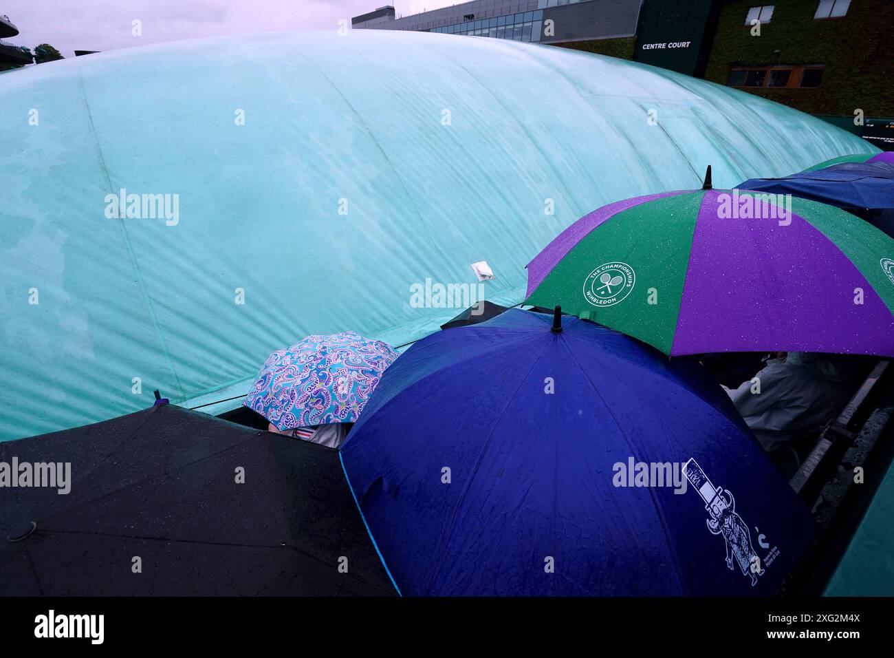 Spectators shelter from the rain under umbrellas on a covered court on ...