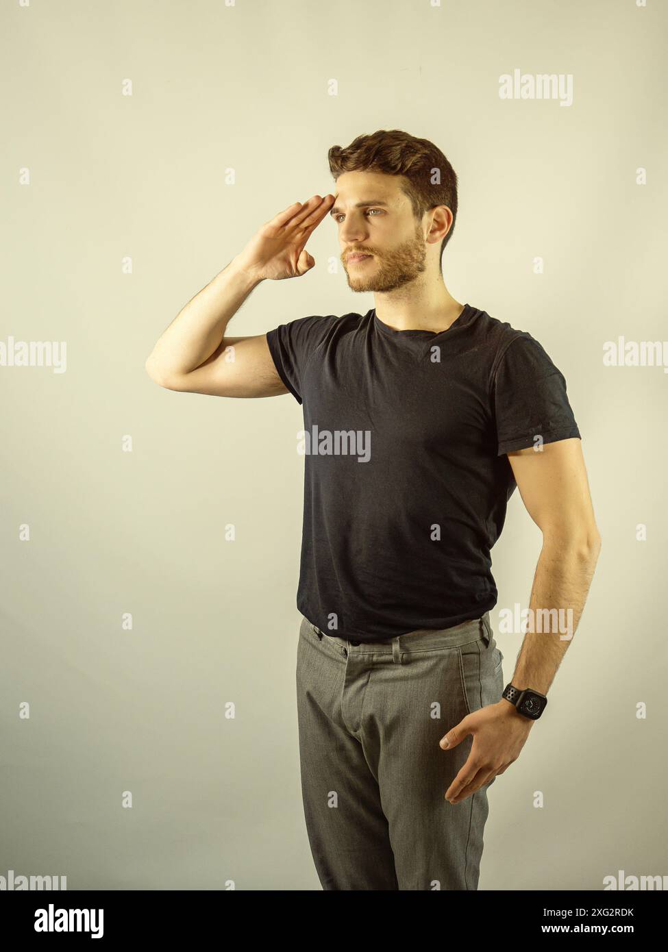 A man wearing a black shirt and grey pants is standing against a plain ...