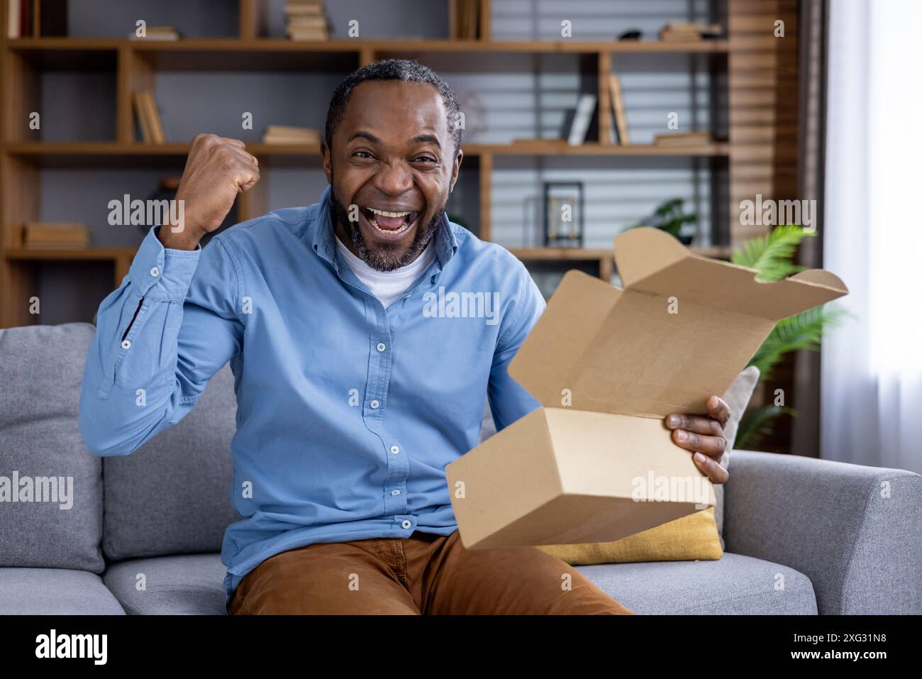A joyful man is excitedly celebrating upon opening a package while ...