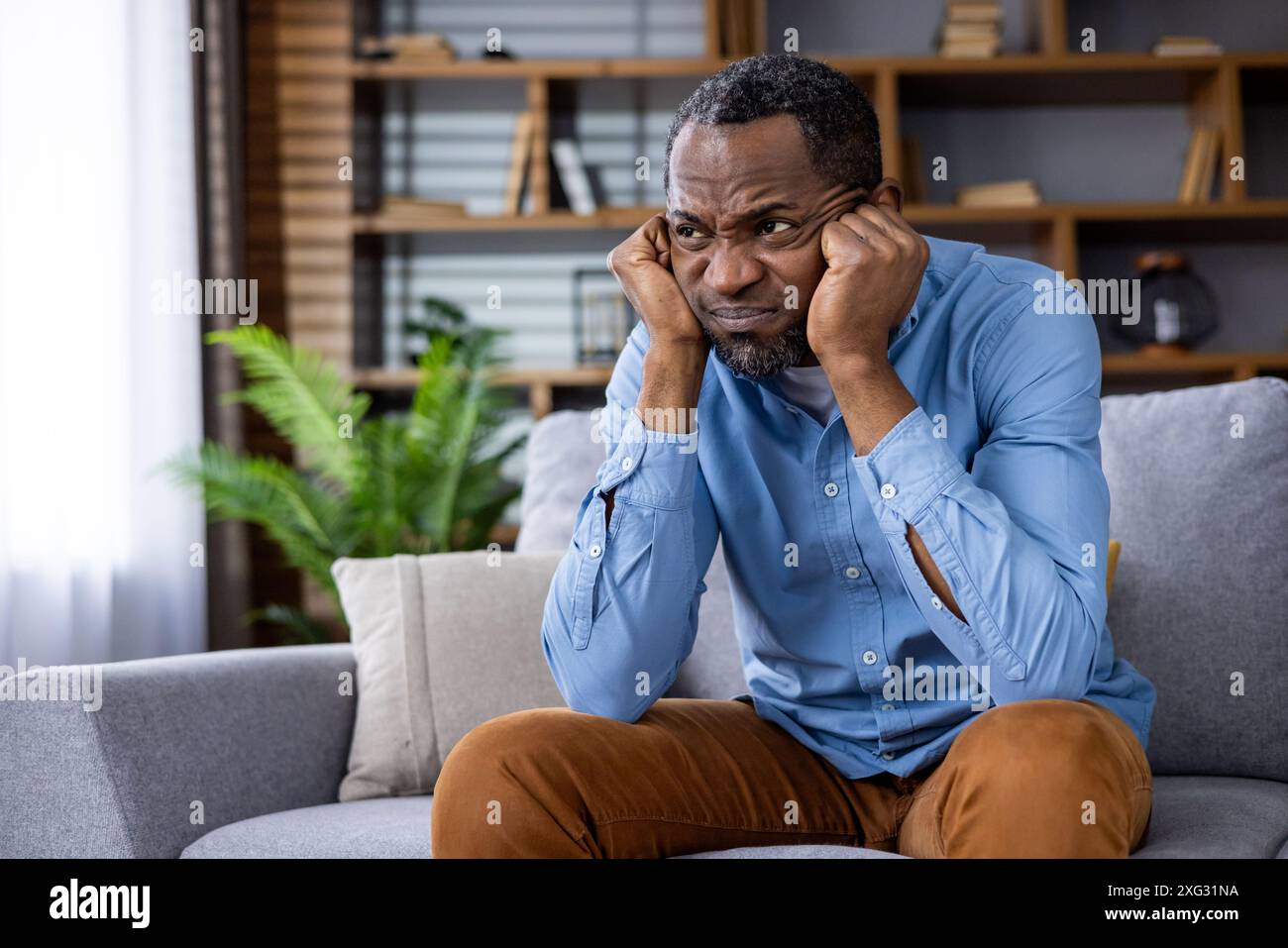 A frustrated man with a distressed expression sits on a couch in a ...