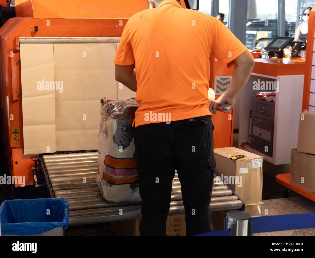 Worker wrapping transparent plastic shrink-wrap onto baggage for ...