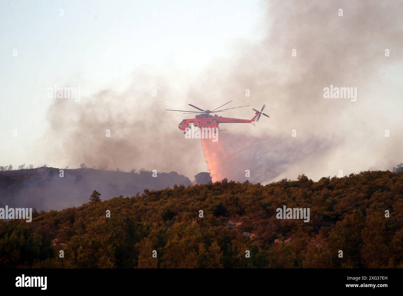 A firefighting helicopter throws water over a wildfire at Keratea area ...
