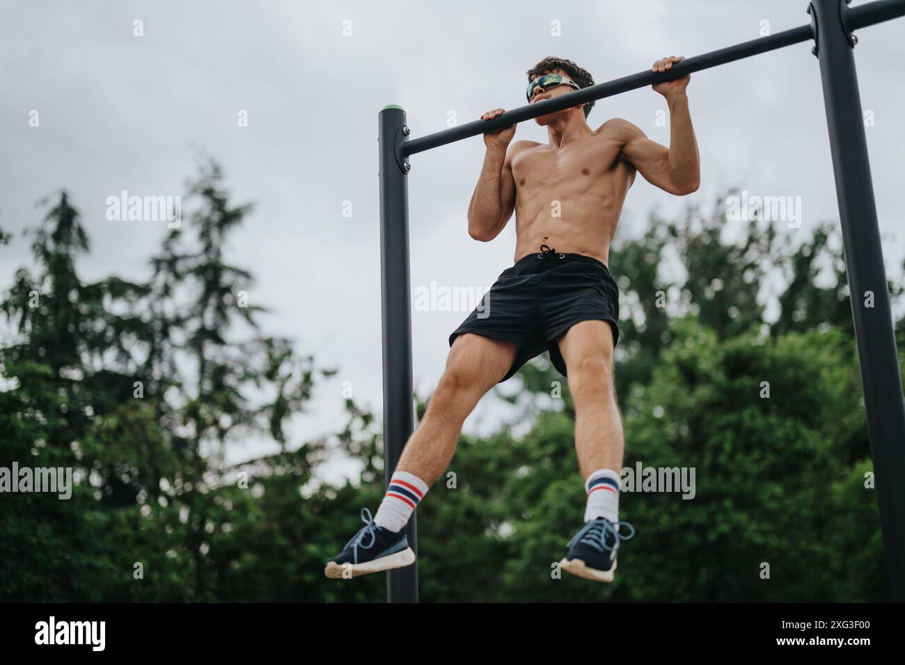 Fit man performing pull-ups on a metal bar in an outdoor park setting ...