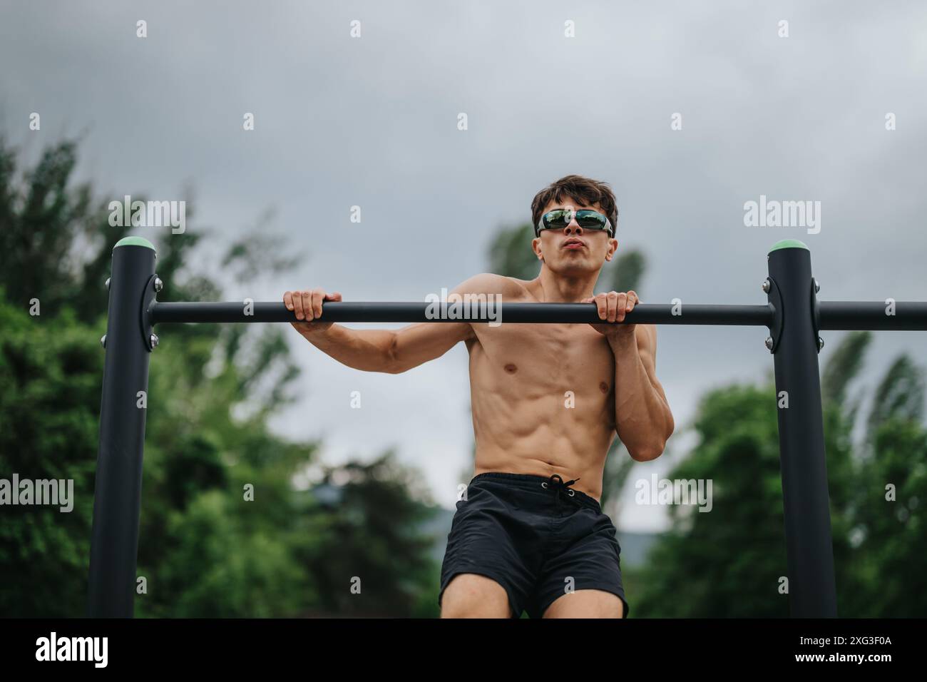 Young man performing pull-ups on outdoor gym equipment, exercising ...