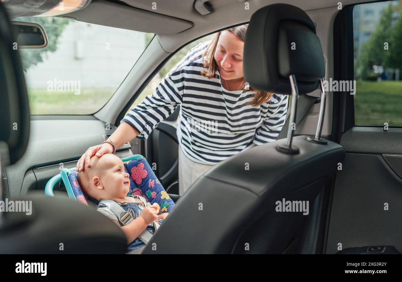 Mother pat on the head her baby in car front seat before driving. Scene ...