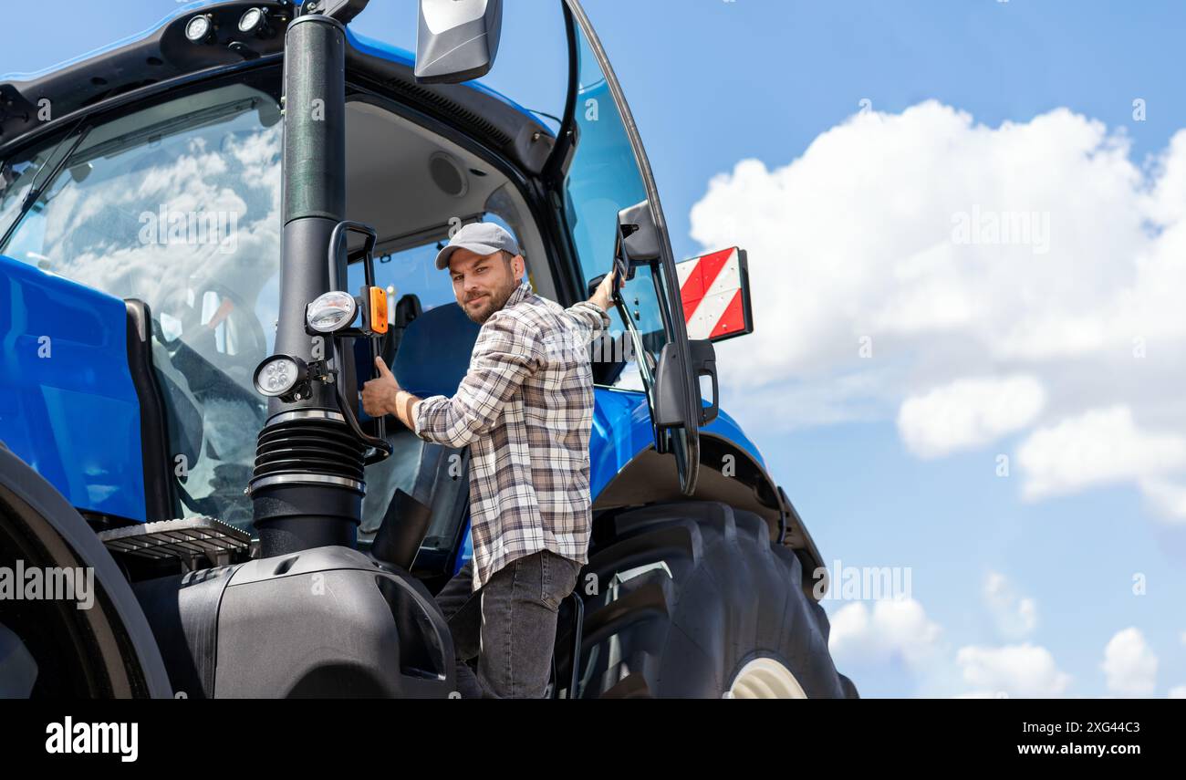 Male tractor driver gets into the blue farm tractor Stock Photo - Alamy