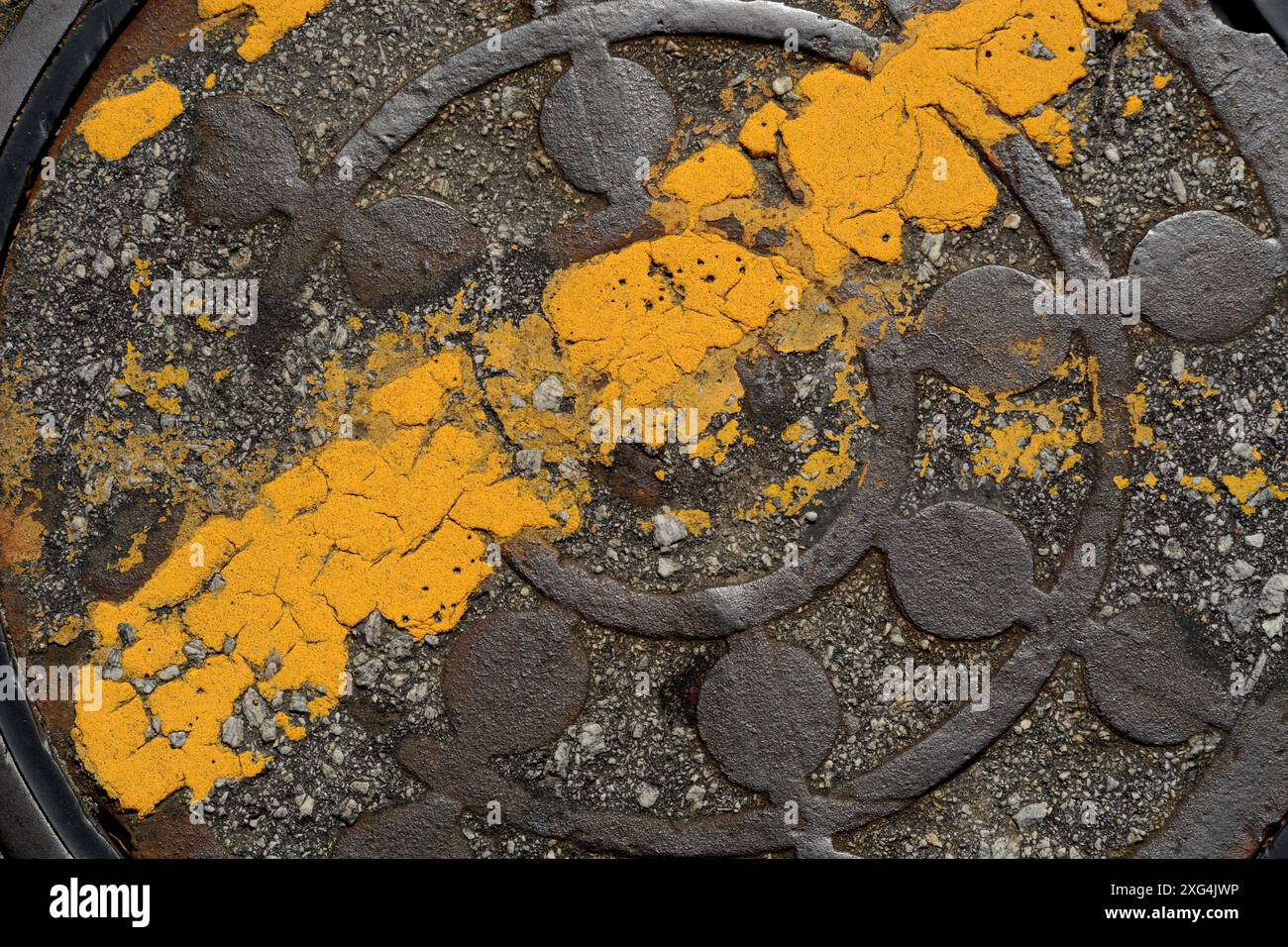 A steel manhole cover covered with asphalt and yellow paint on a ...