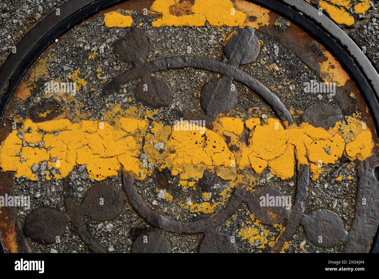 A steel manhole cover covered with asphalt and yellow paint on a ...