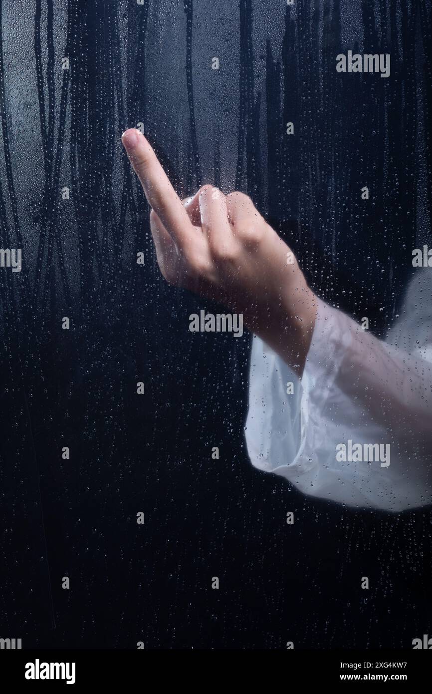A man hand gesturing to the camera behind wet glass. Studio portrait ...