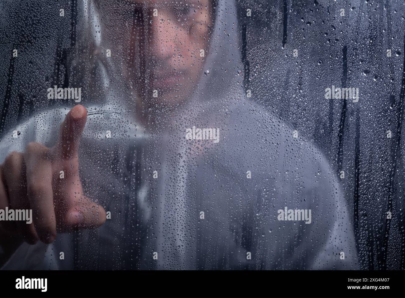 Portrait of a man wearing a raincoat behind a wet glass writing the ...