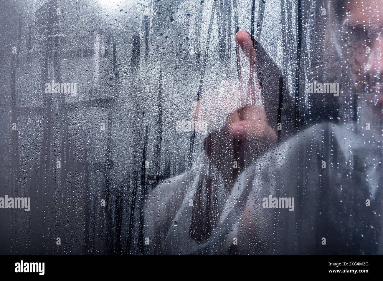 Portrait of a man wearing a raincoat behind a wet glass writing the ...