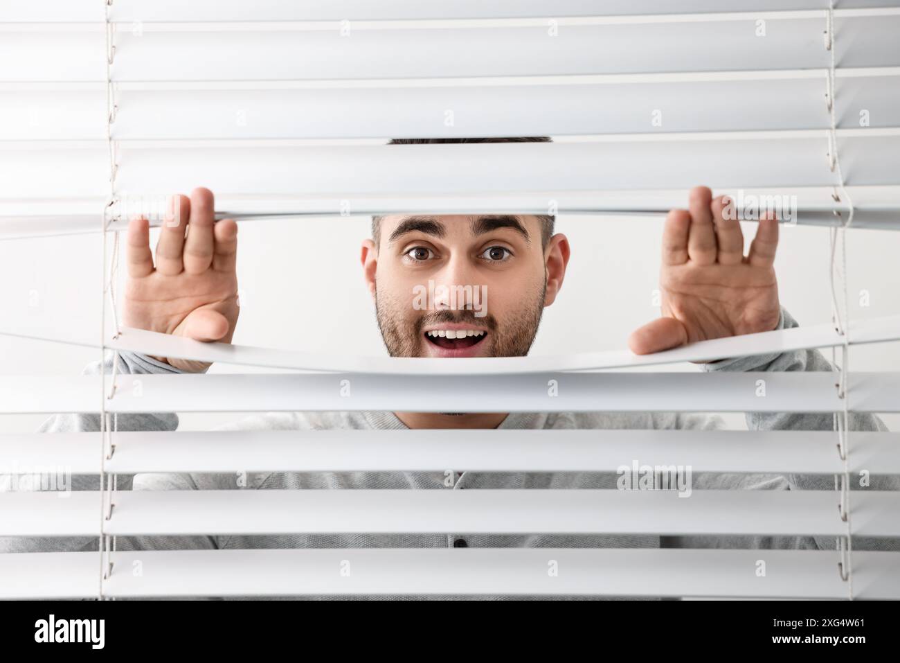 Young man looking through window blinds on white background Stock Photo ...