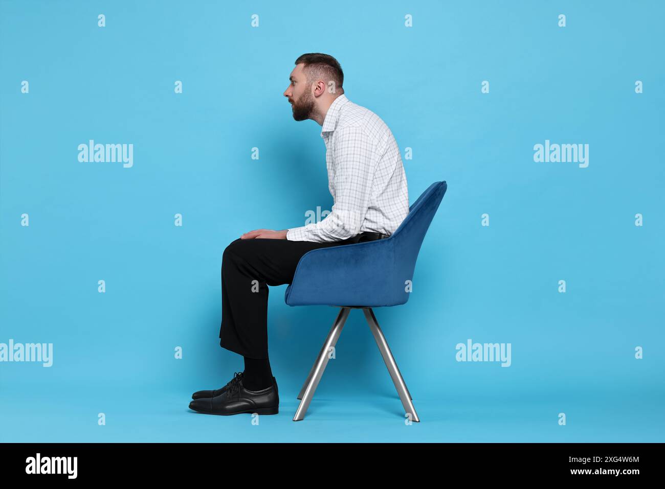 Man with poor posture sitting on chair against light blue background ...