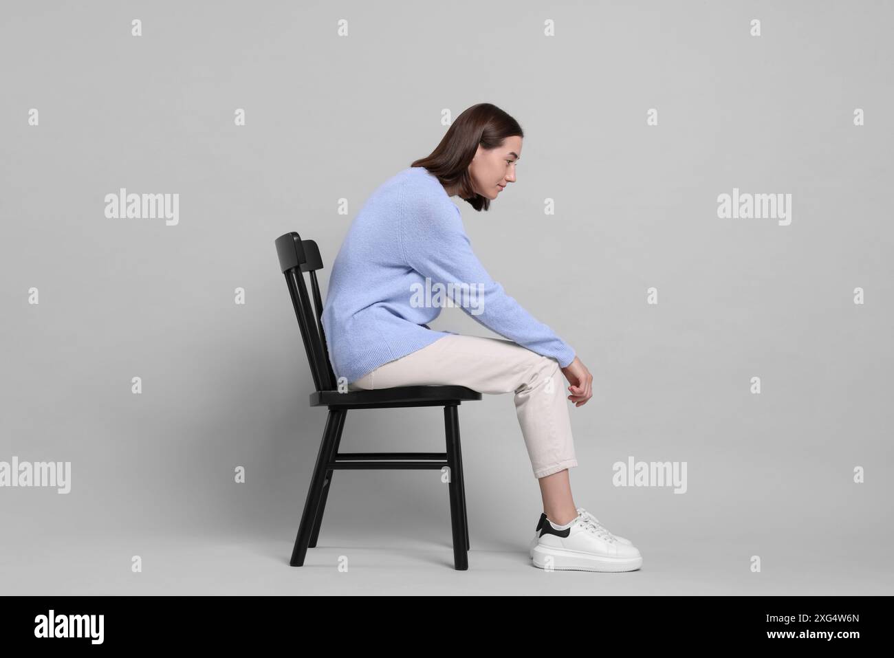 Woman with poor posture sitting on chair against gray background Stock ...