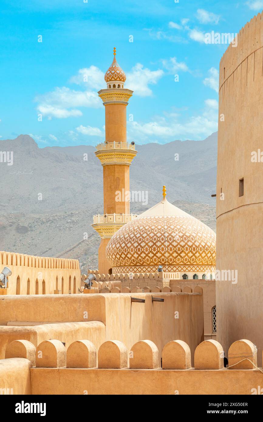 Al Qala'a Mosque ornated dome and minaret with Nizwa castle walls in ...