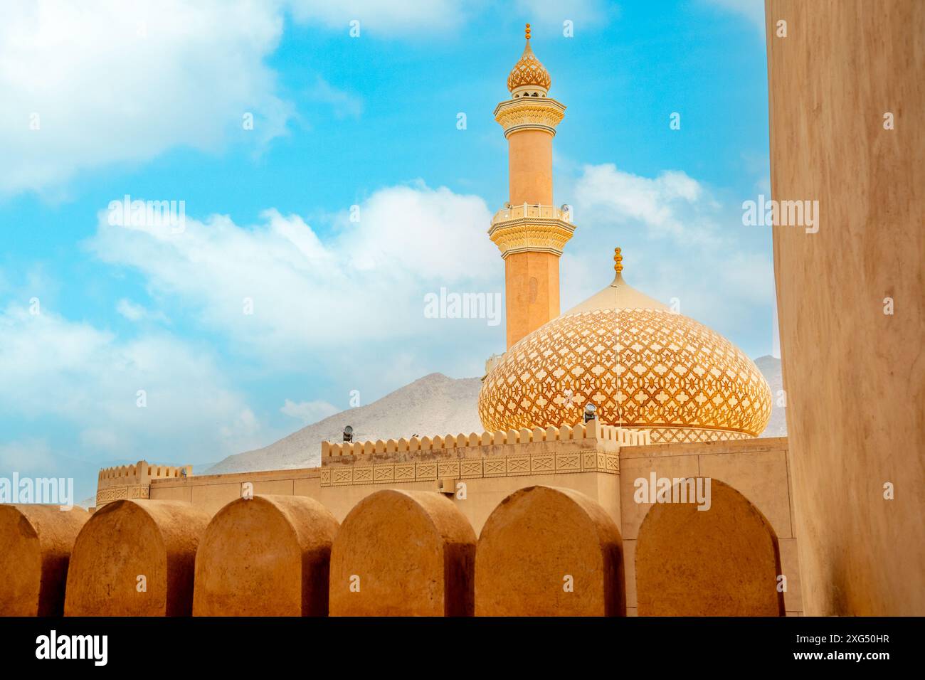 Al Qala'a Mosque ornated dome and minaret with Nizwa castle walls in ...